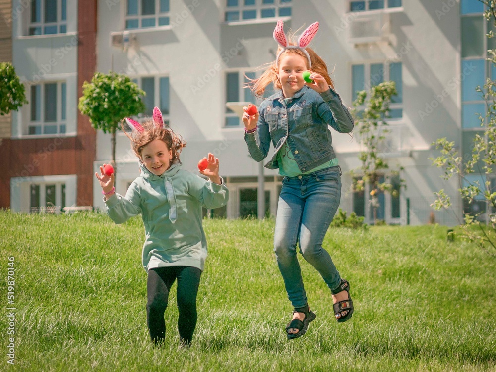 Funny naughty girls are jumping on the green grass with an Easter egg ...