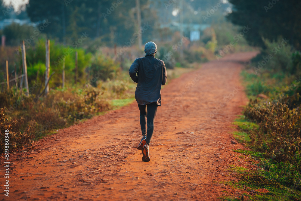 A lone runner trains in Kenya. A marathon runner runs on red soil in ...
