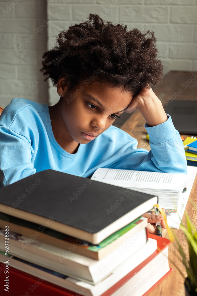 Sad bored African-American girl doing homework at home at her desk.Back ...