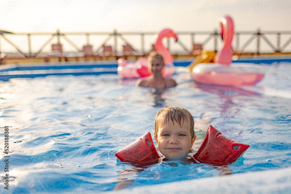 A boy with armbands and a disgruntled face, trying to get out of a pool ...