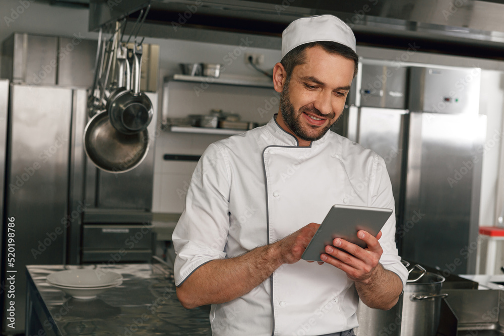 Smiling chef in uniform making order in digital tablet for the supplier ...
