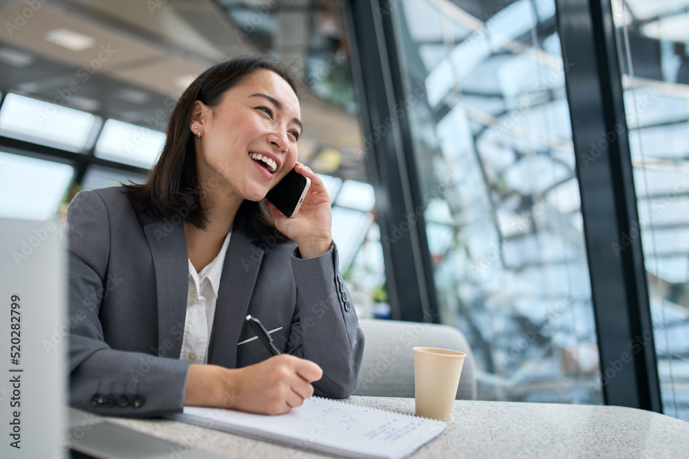 Cheerful young chinese business woman talking on phone working in ...