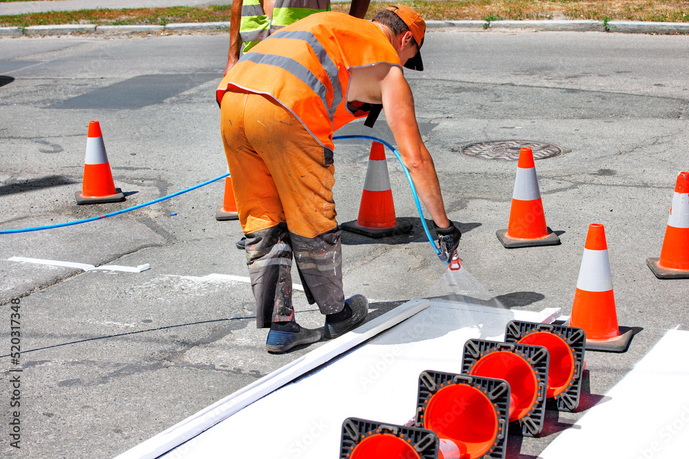 Road workers mark a pedestrian crossing on the roadway with white paint ...