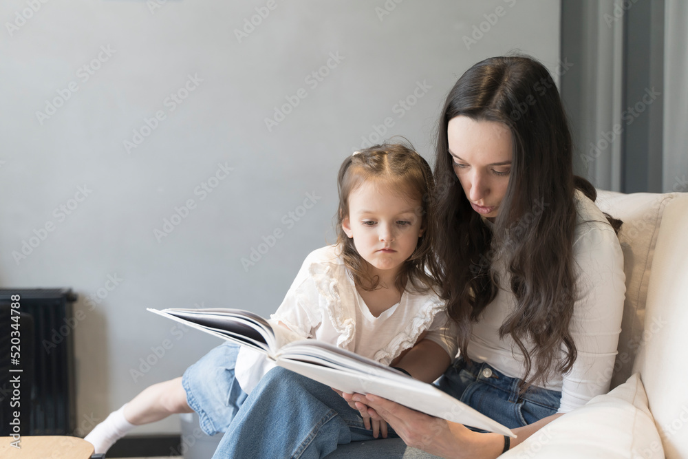 Mom and daughter are reading a book on the sofa. Study and activities ...