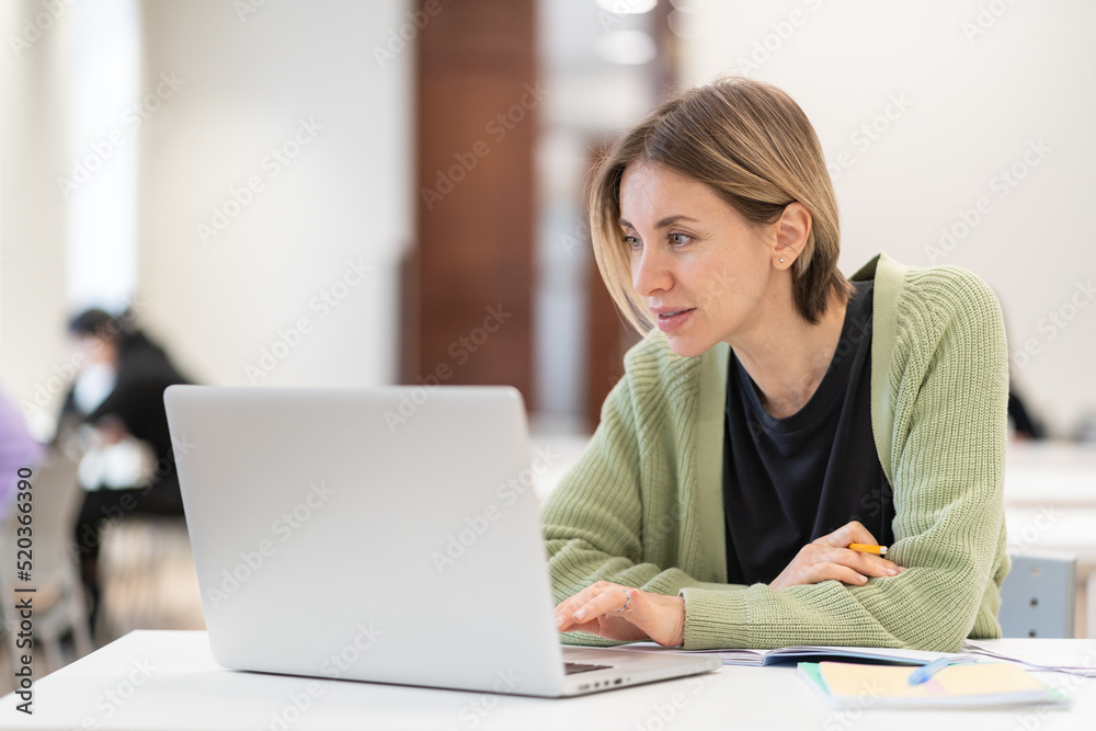 Smiling middle-aged woman studying online on laptop computer while ...