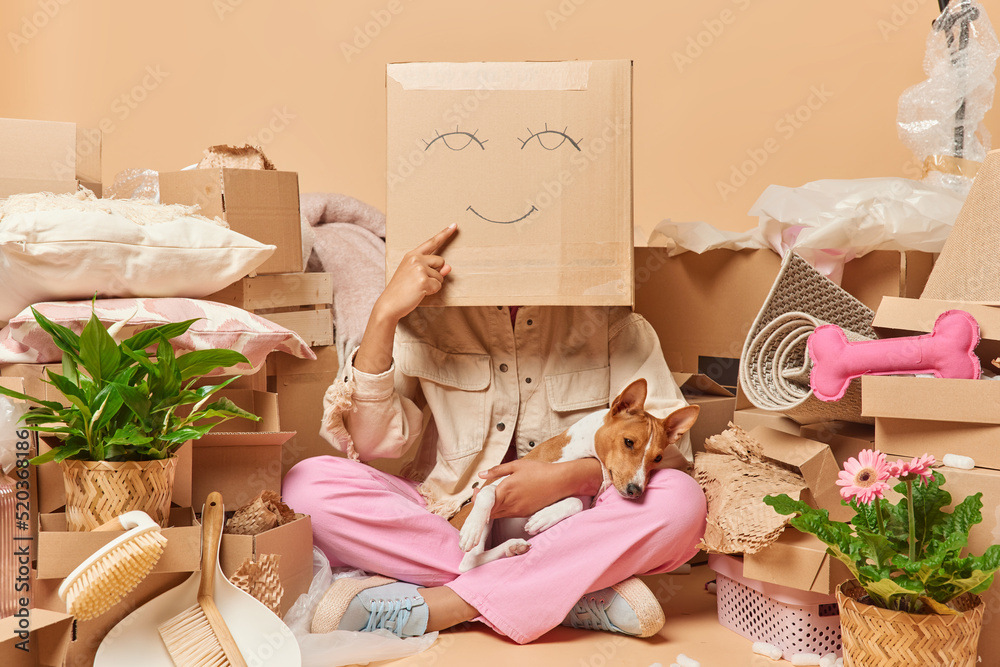 Foto de Faceless woman hides behind carton box foolishes around poses ...