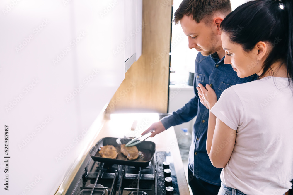 cute couple hugging in the kitchen while cooking steak for dinne Stock ...