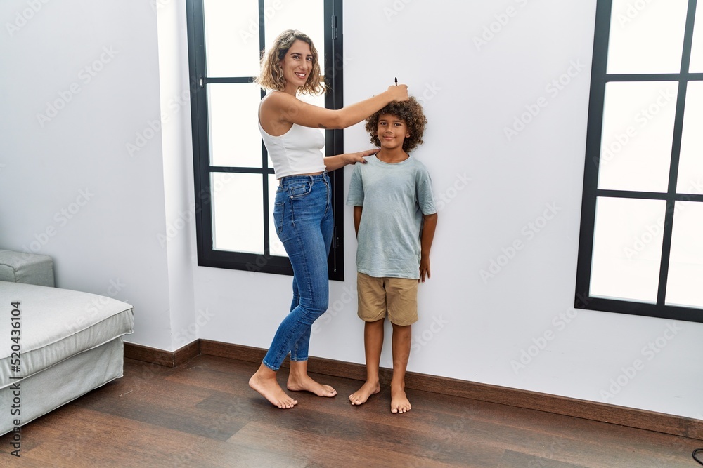 Mother and son measuring child height drawing mark on wall at home ...