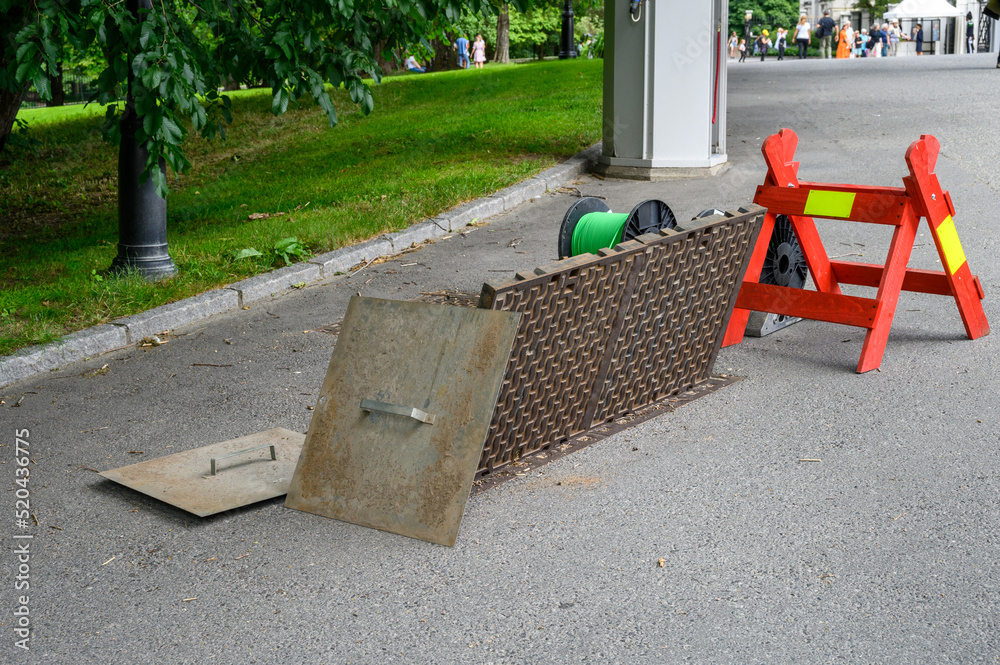 Open equipment vault in a street next to a park, orange safety barrier ...