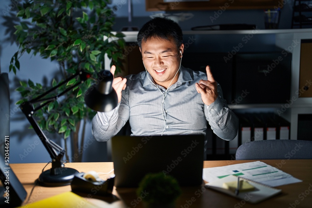 Young chinese man working using computer laptop at night shouting with ...