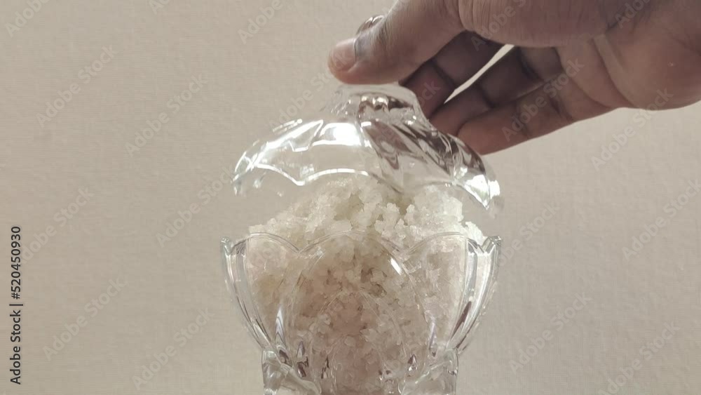 Hand opening hinged lid cover of glass bowl filled with raw white bath ...