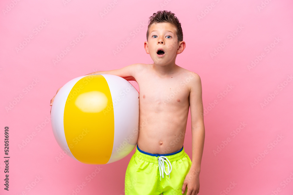Little caucasian boy holding a beach ball isolated on pink background ...