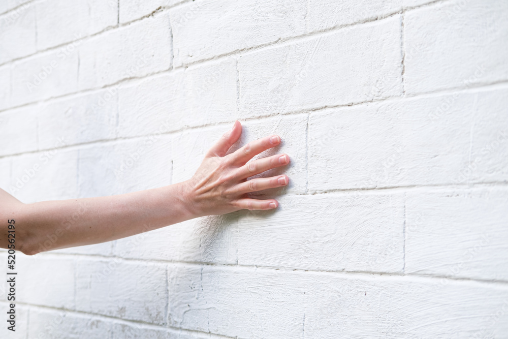 Woman's hand on the background of a white brick wall. A woman touches ...