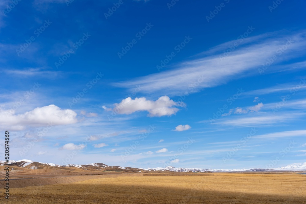 Dry desert under a blue sky with clouds with snow-peaked mountains in ...