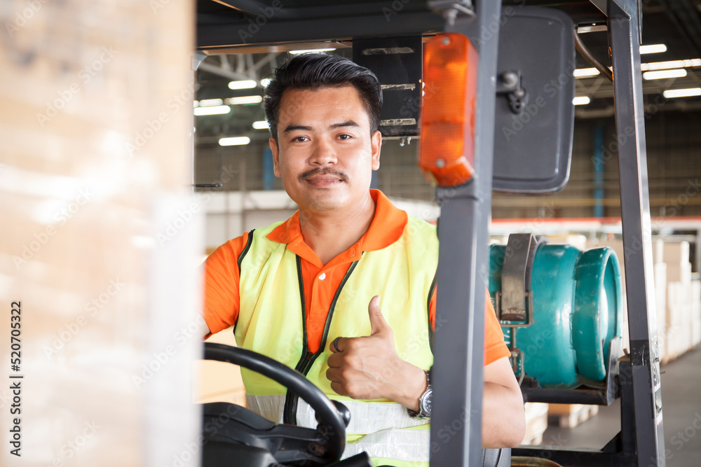 Happy and satisfied Asian worker in warehouse sitting a forklift and ...