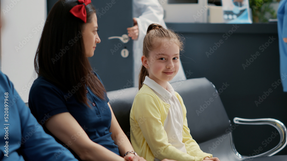 Portrait of little girl waiting with mother at hospital reception lobby ...