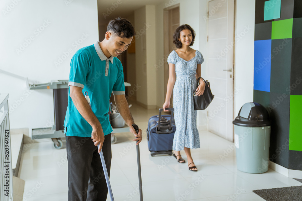 Janitor wearing turquoise uniform sweeps as female guests walk past in ...
