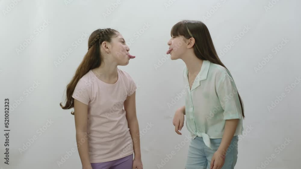 Two little girls stick out tongues at each other on white background ...