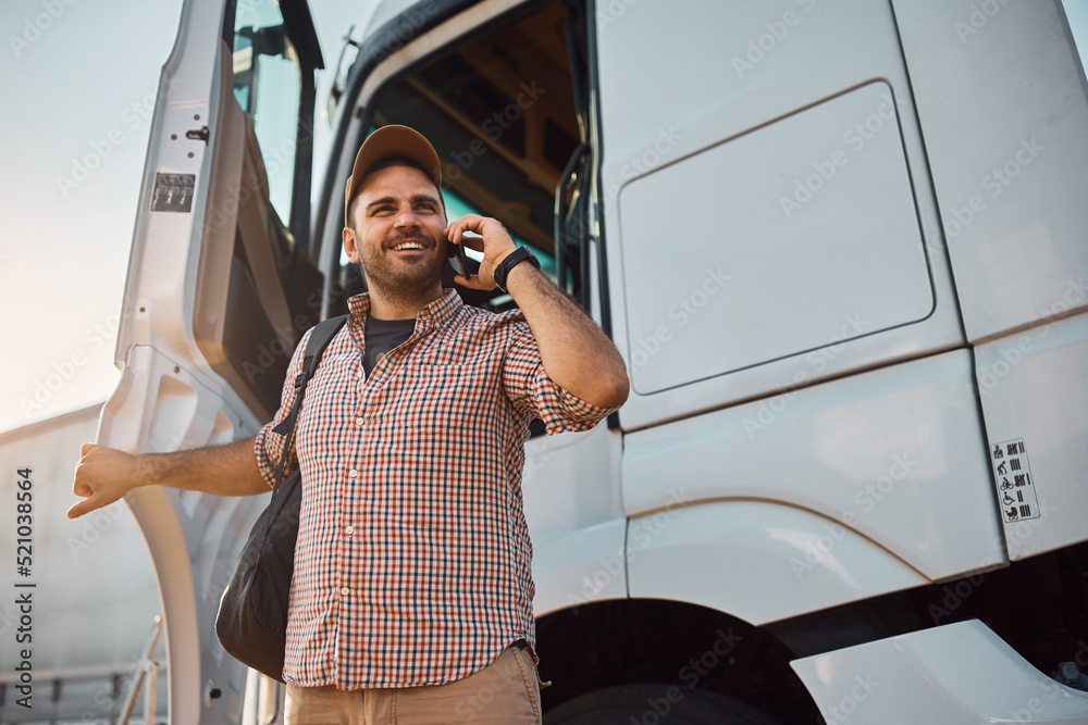 Happy truck driver communicating on mobile phone while getting out of ...