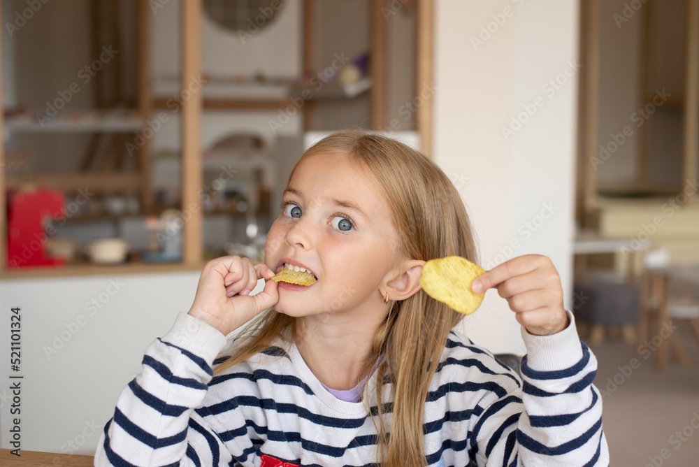 Caucasian little girl puts a snack in her mouth with her hand. The ...