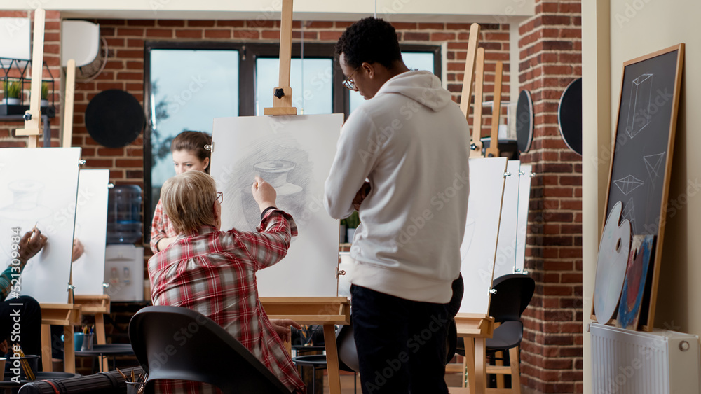 Man and woman giving advice to elder student in art class, drawing vase ...