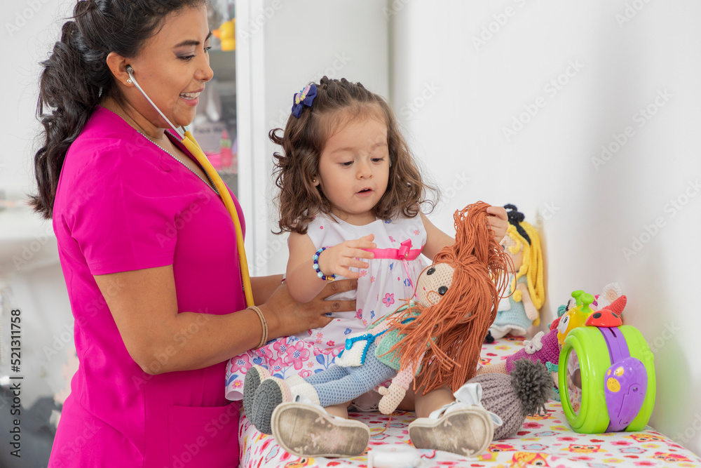 Girl playing with a doll in the office, while the doctor checks her ...