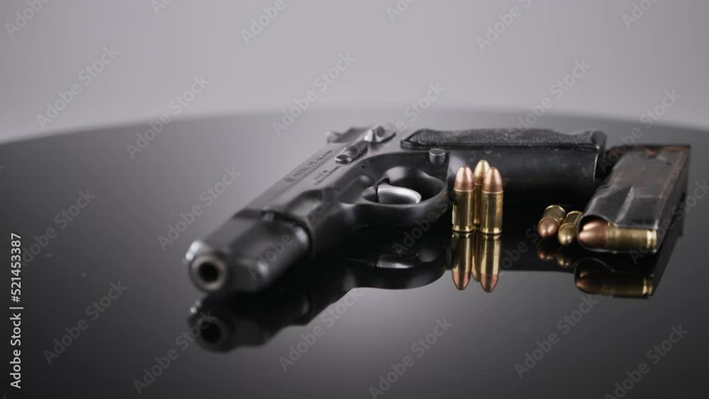 Gun Control. 9mm handgun with bullets rotating on a reflective surface ...