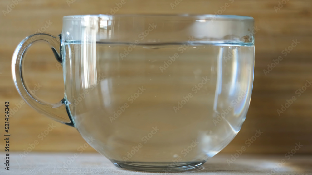 Pouring hot water into a big transparent cup on blurred wooden ...