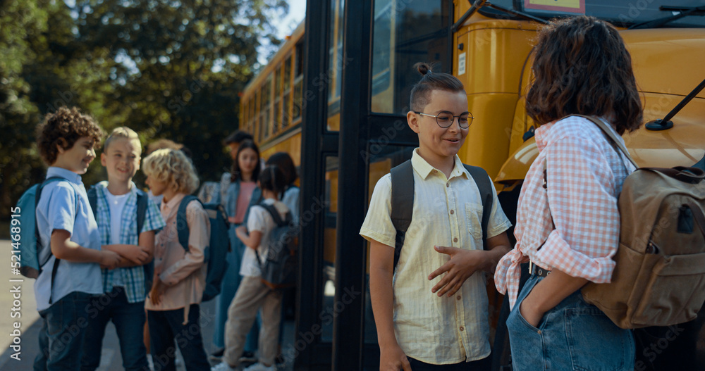 Students waiting schoolbus boarding. Pupils standing talking at yellow ...