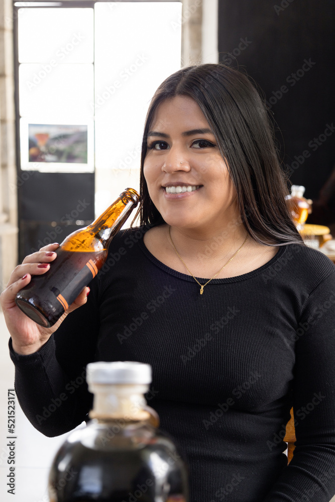 cheerful latin young woman holding a bottle of beer to toast, she has ...