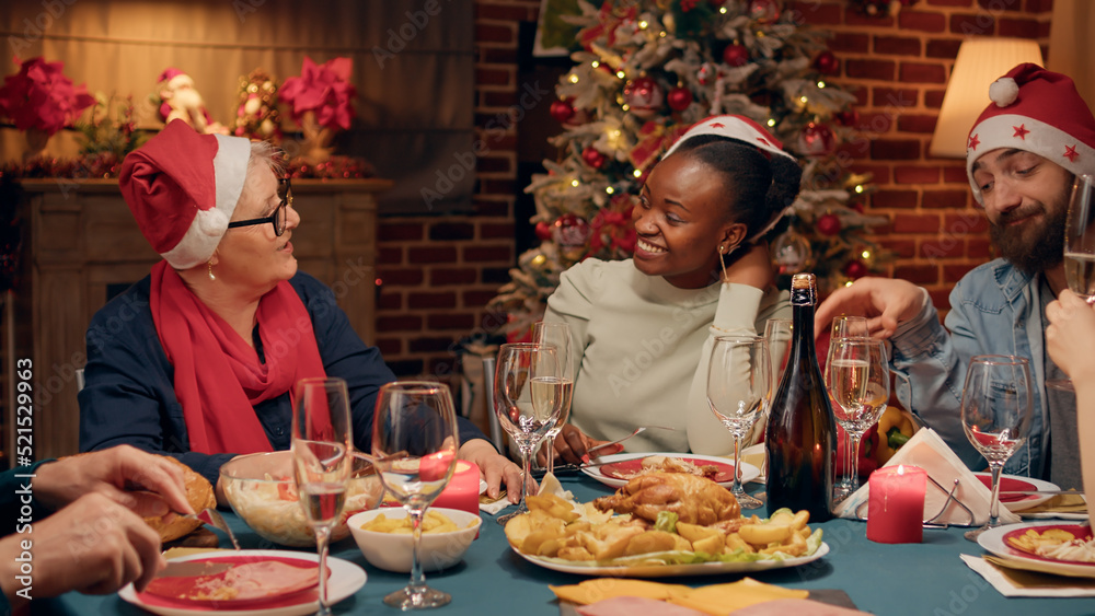 Cheerful diverse women talking at Christmas dinner table while enjoying ...