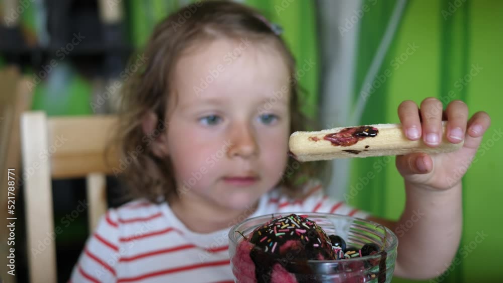 Cute little girl eat a biscuit with ice cream in a restaurant sitting ...