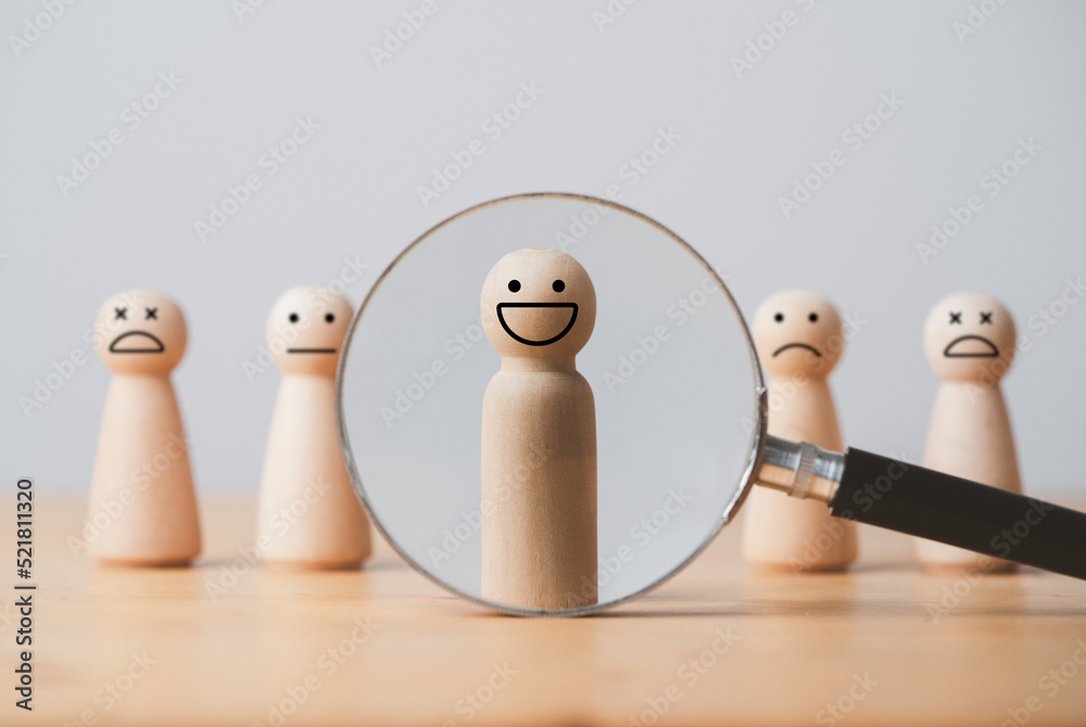 Smile face of wooden figure inside of magnifier glass among sad face ...