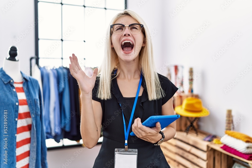 Young blonde woman working as manager at retail boutique crazy and mad ...