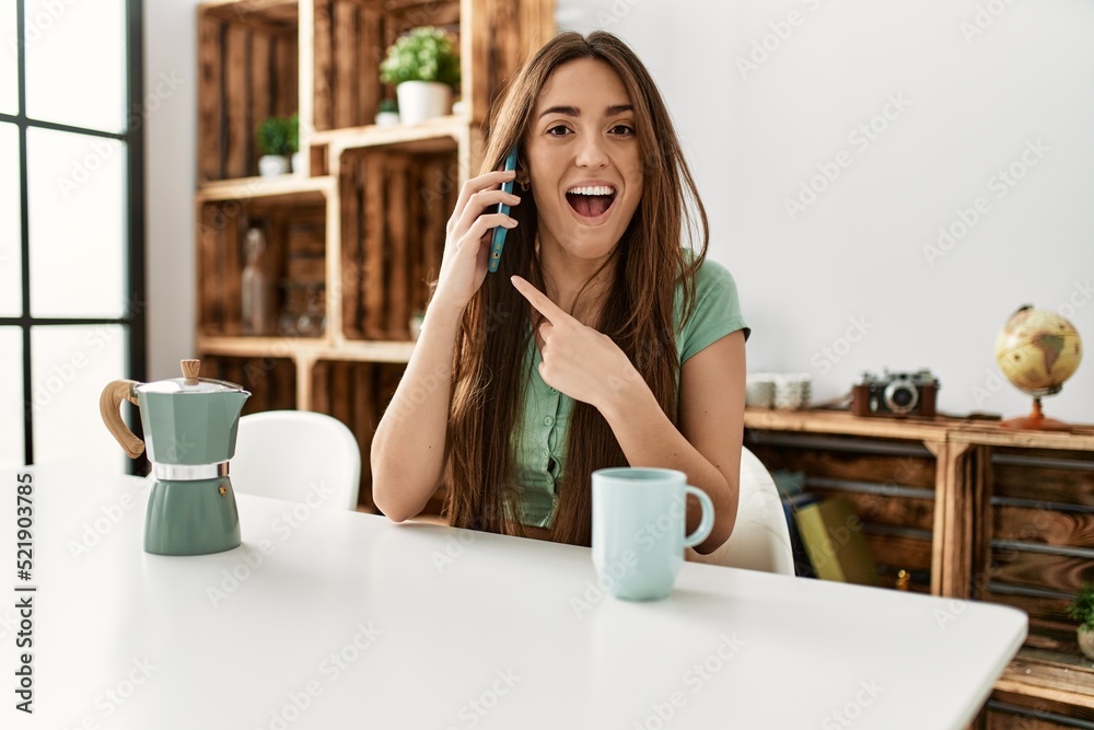 Young hispanic woman talking on the smartphone sitting on the table at ...