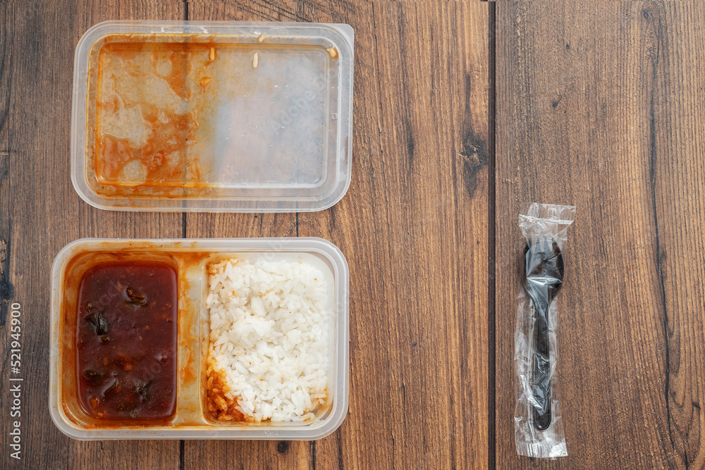 Fast food in a plastic container and small plastic fork on a wooden ...