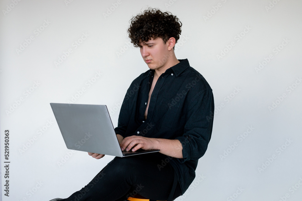 Handsome young curly guy in total black look sitting on chair and ...