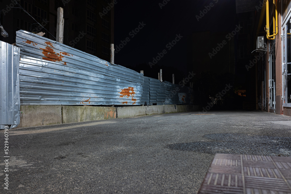 Dark empty alley with galvanized steel fence with wooden pillars in ...