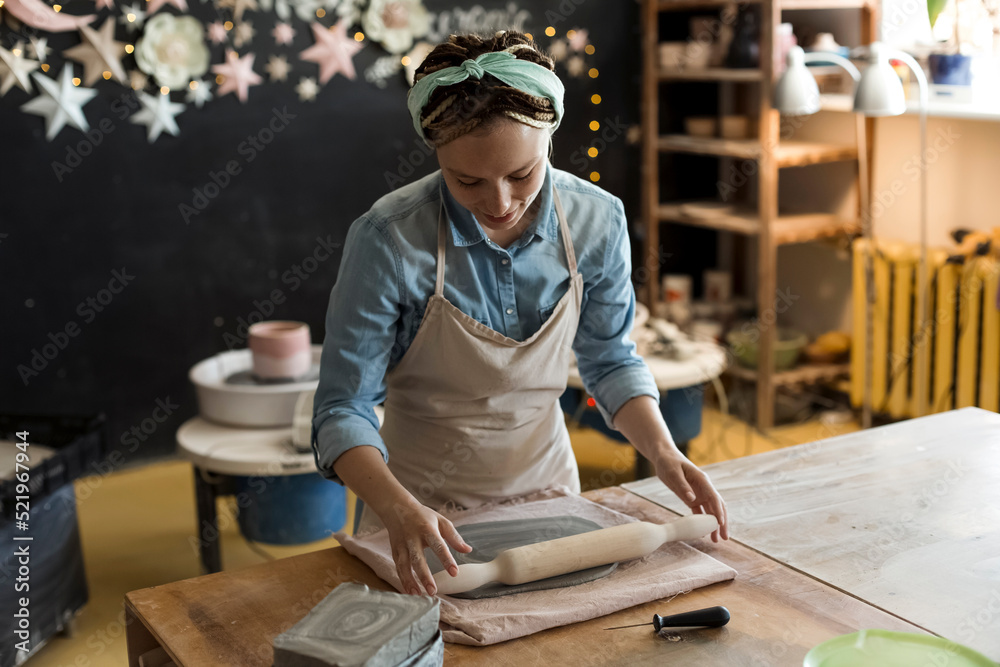 Smiling craftsperson rolling clay with pin on workbench at art studio ...