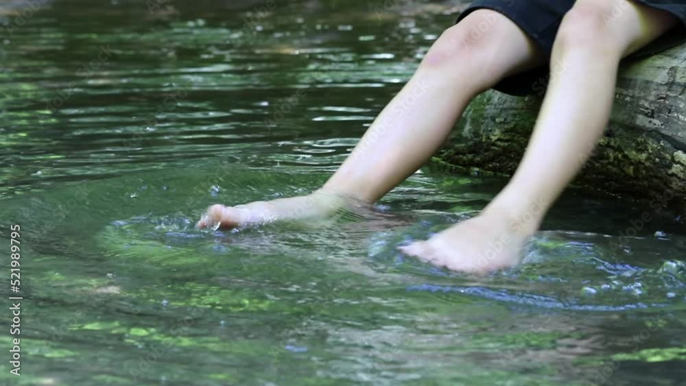 Barefooted boy cooling his feet in water with crystal clear water and ...