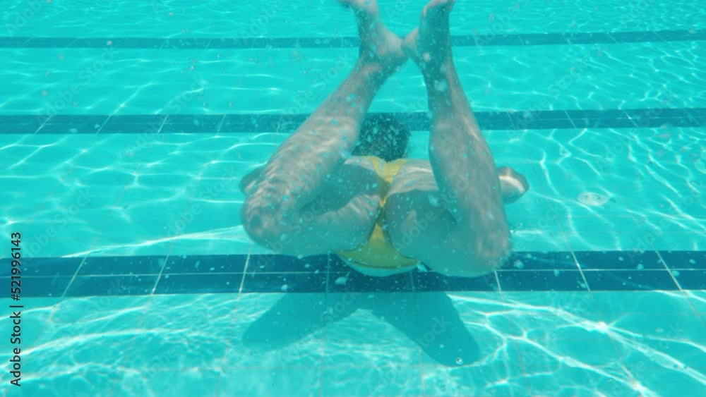 A chubby girl in a yellow swimsuit and long hair, pushes off and swims underwater, the camera ...