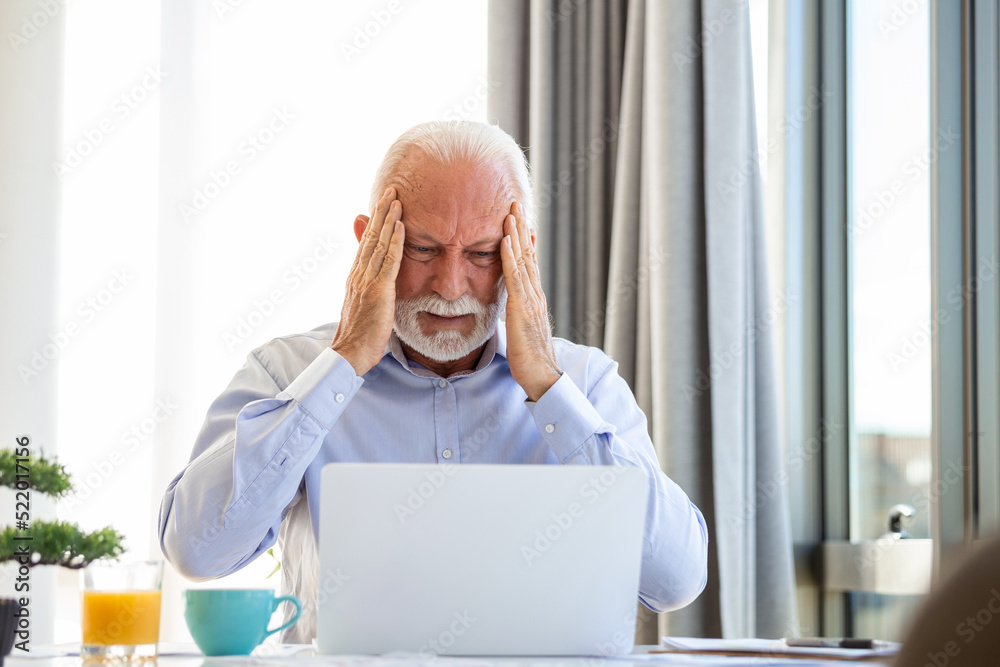 Stressed mature businessman with laptop. He could also have a headache ...