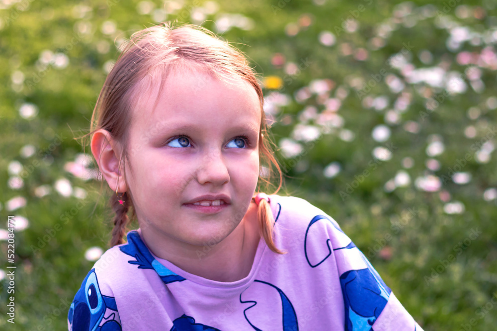 girl of 7-8 years old sits against the backdrop of a green flowering ...