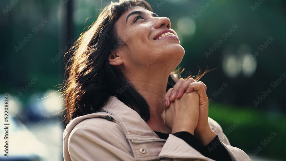 A grateful hispanic woman praying to God with hands clenched looking at ...