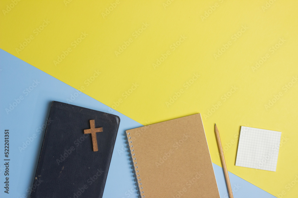 Bible with notebook with pencil over the yellow and blue background ...