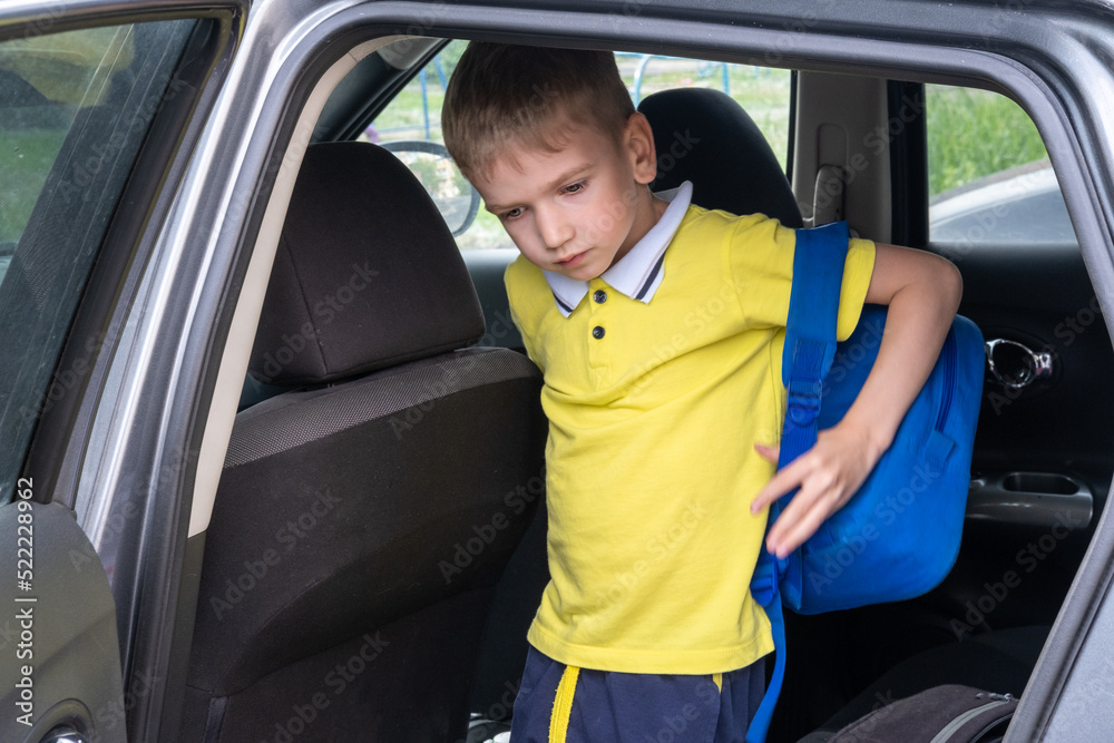 Portrait of a smiling boy with a school bag getting out of the car ...