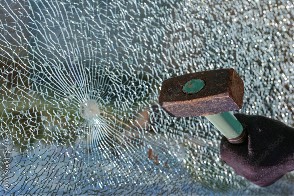 Hand With A Hammer And A Broken Window Made Of Safety Glass Concept For Burglary And Vandalism