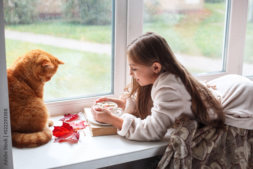 Little girl with red cat lying on window sill , reading a book and ...