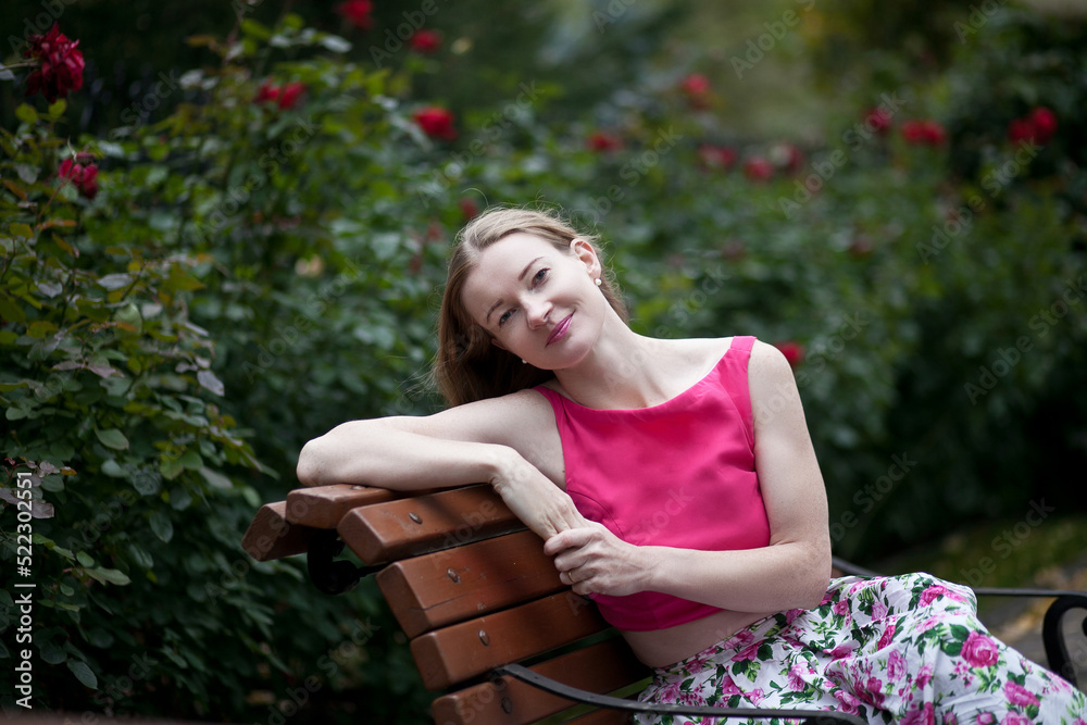 Beautiful woman with long blond hair. A woman walks in a rose garden ...