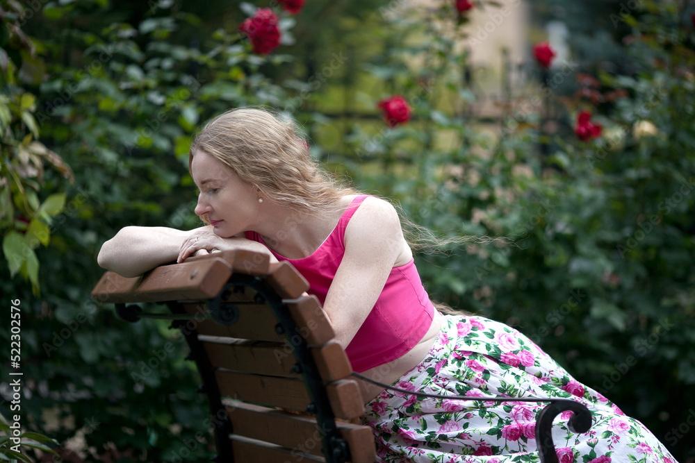Beautiful woman with long blond hair. A woman walks in a rose garden ...